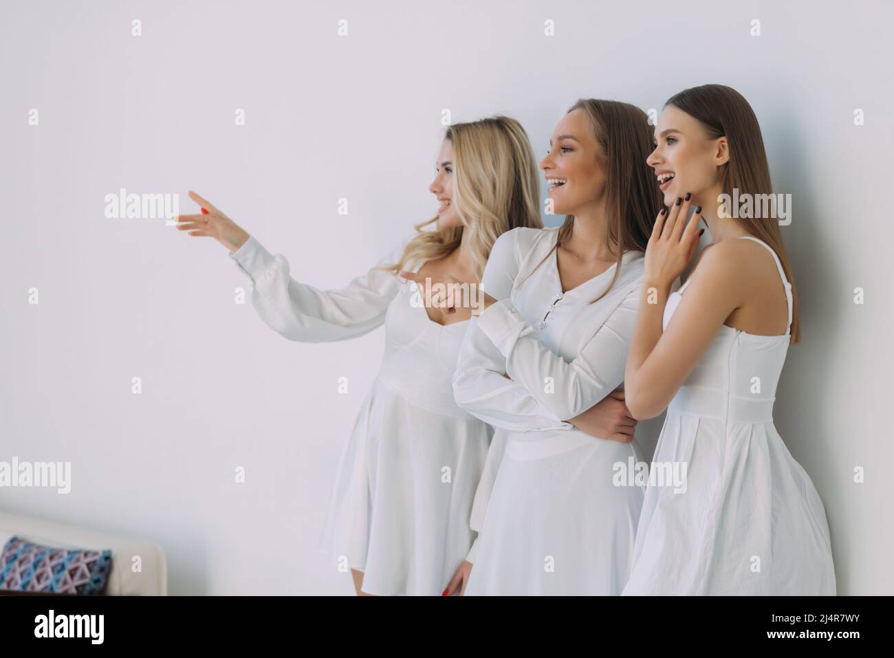 Pleased three women smiling pointed side over white wall Stock Photo ...
