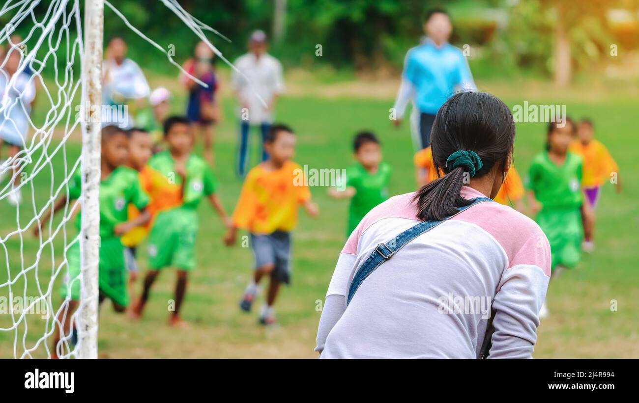 Back view of Mom watch and cheering her son playing football in school ...