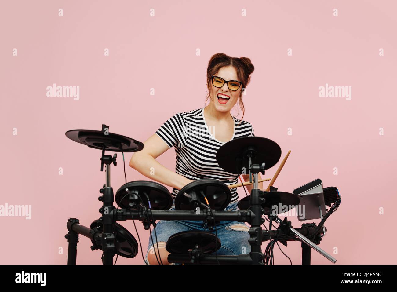 Energetic eccentric lady playing on electric drums. Over pink ...