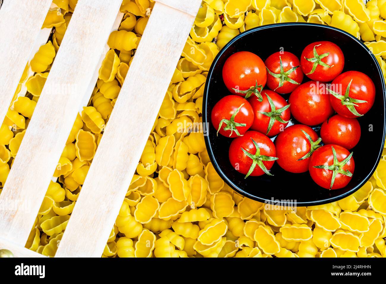 Top view of pasta in a wooden crate and fresh ripe cherry tomatoes in a ...