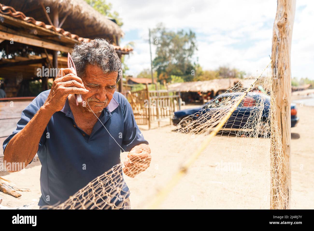 Elderly Latino fisherman weaving a cast net used to hunt squid in a ...