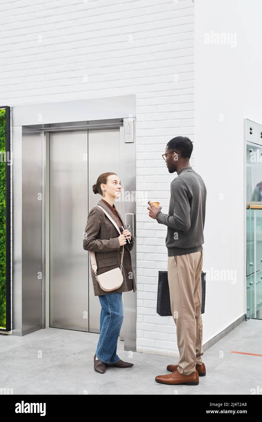 Vertical full length portrait of two coworkers chatting by elevator in ...