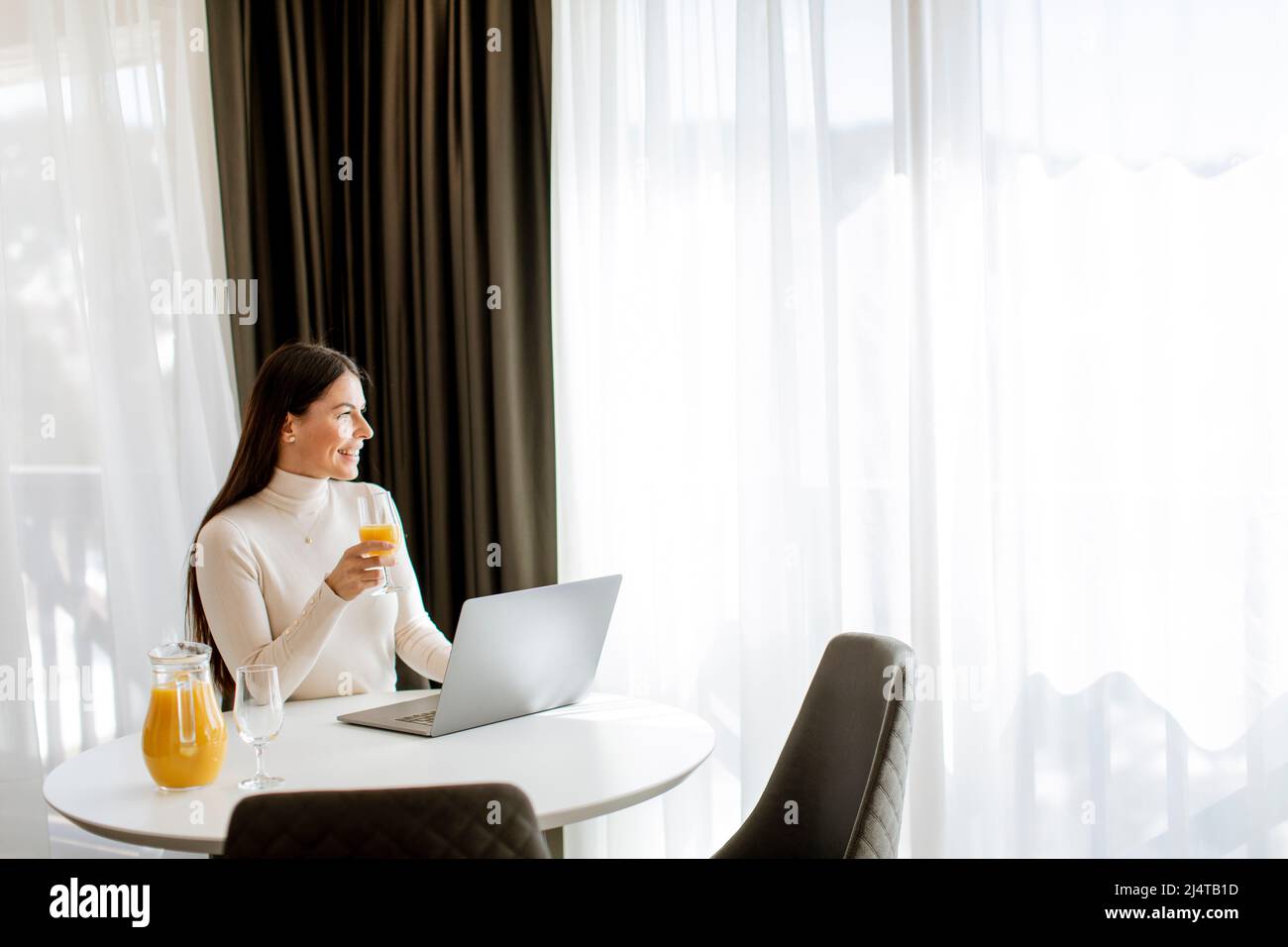 Young woman using a laptop computer and drinking healthy orange juice ...