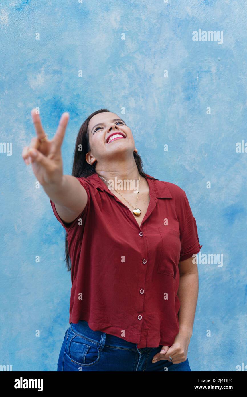 woman showing peace sign while standing by wall Stock Photo - Alamy