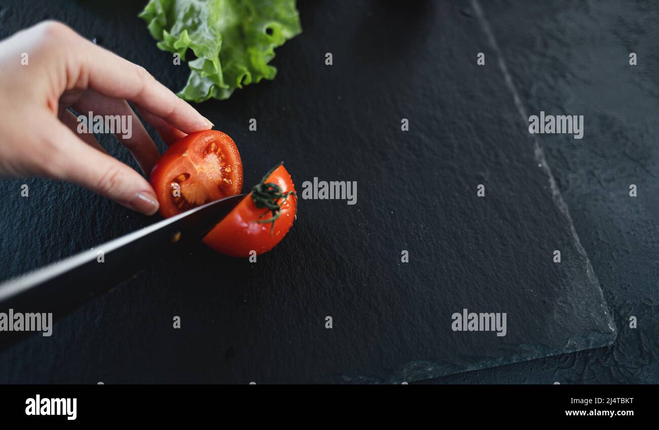 woman cutting and chopping tomato by knife on black slate board. fresh ...