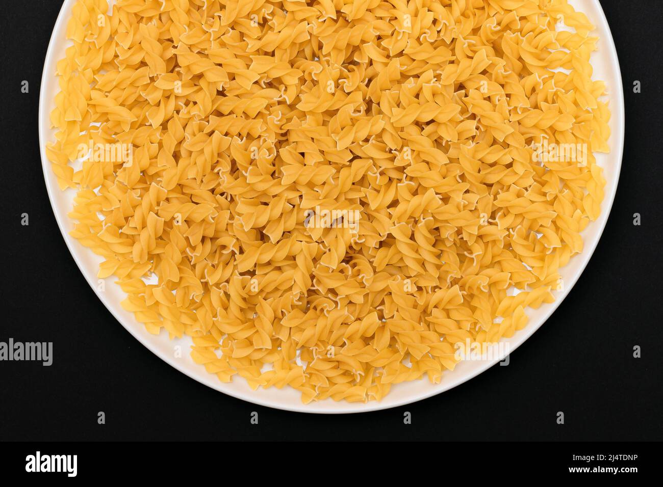 Uncooked Fusilli Pasta Lying on White Plate on Black Background. Raw ...