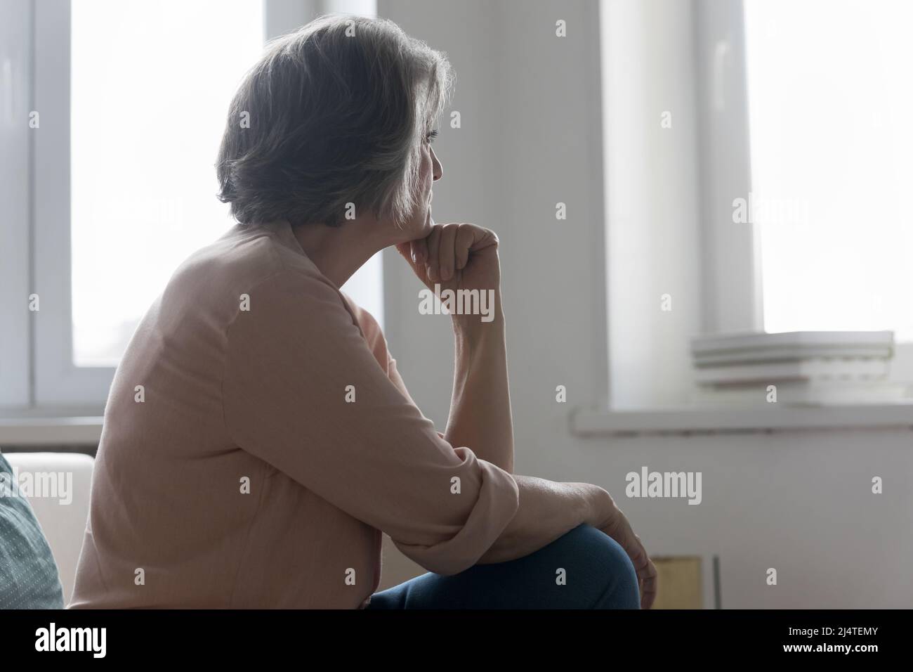 Older 50s woman staring out window sit on sofa indoors Stock Photo - Alamy