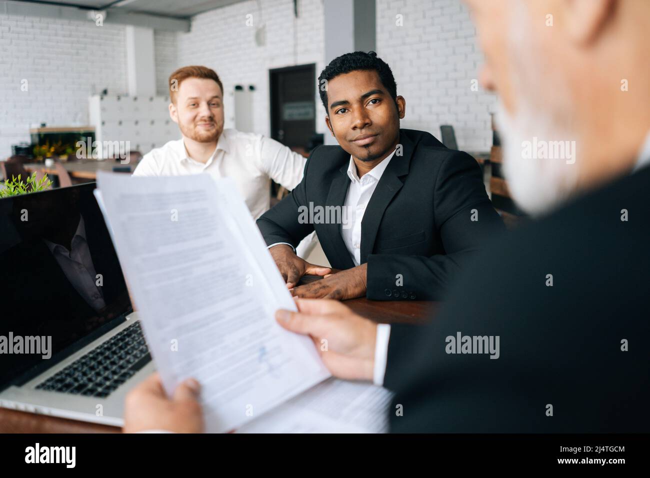Senior adult businessman sitting at desk with multi-ethnic partners ...