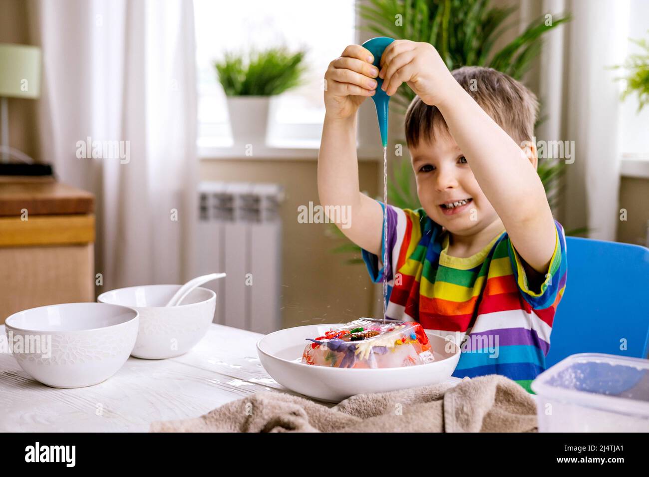 A cute little child pours warm water over toys frozen in ice. Dinosaur ...
