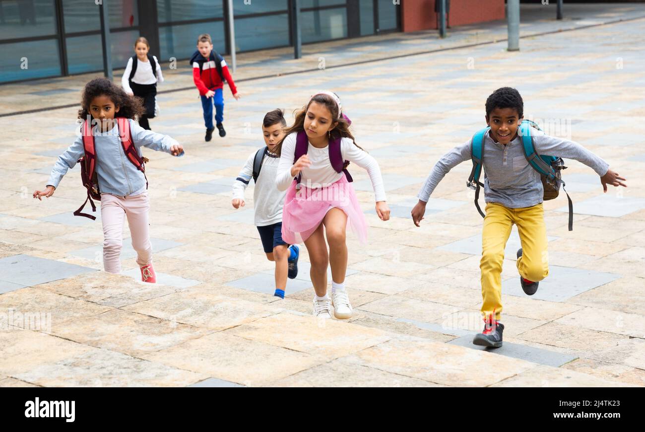 Happy tween schoolchildren with backpacks running to school outdoors ...