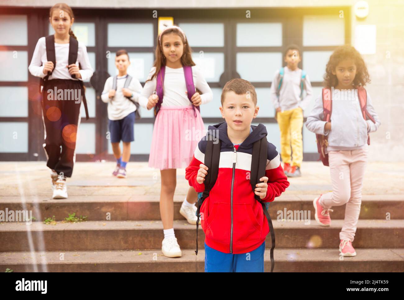 Positive boy standing near school, children on background Stock Photo ...