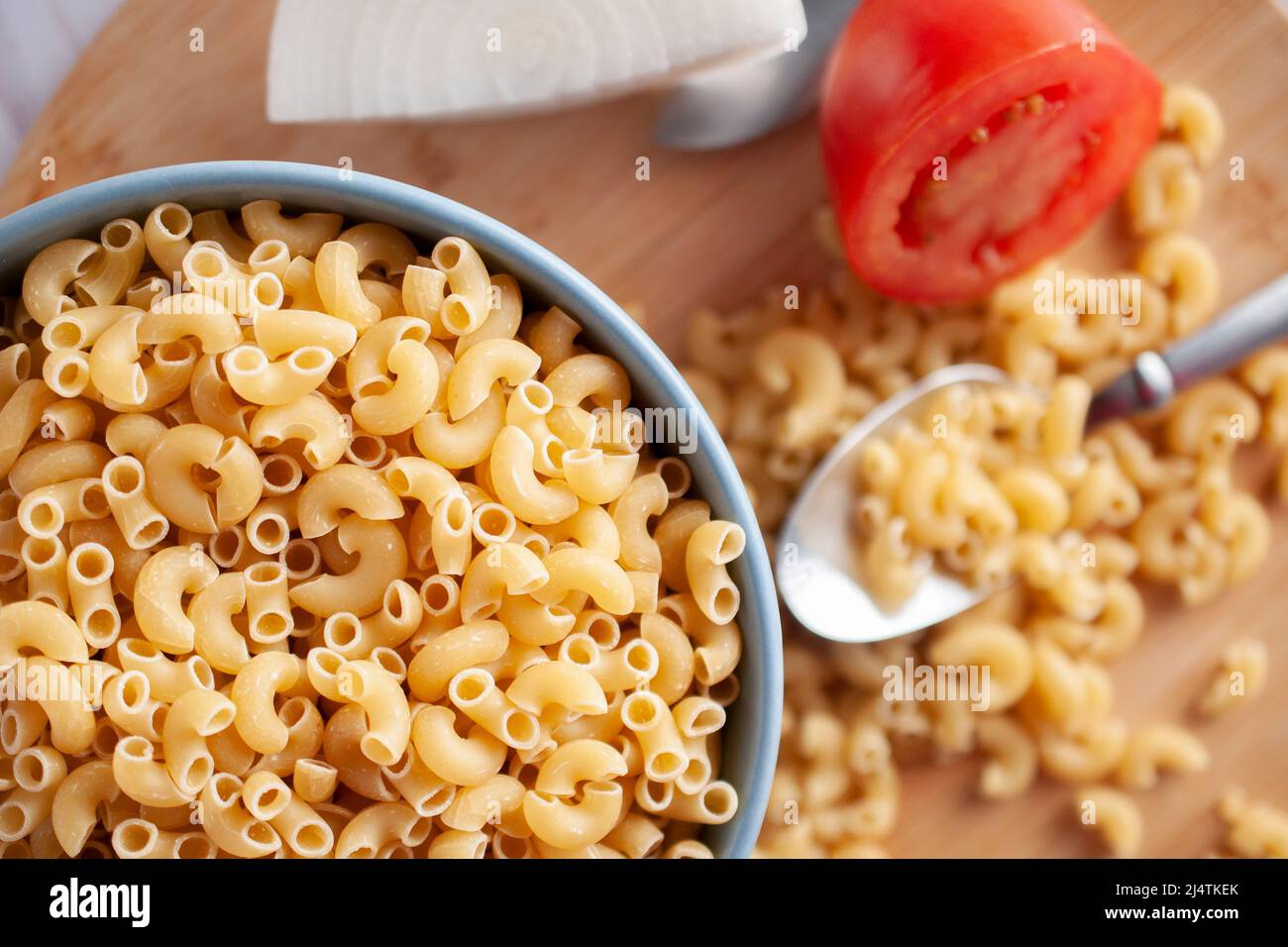 Raw or uncooked Elbow Pasta in a blue bowl and on a wooden chopping ...
