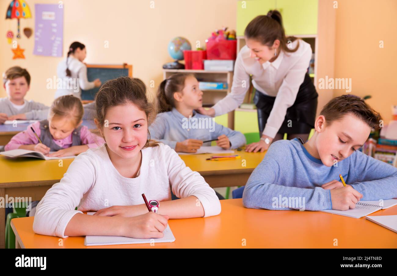 Teacher woman helping children during lesson in schoolroom Stock Photo ...