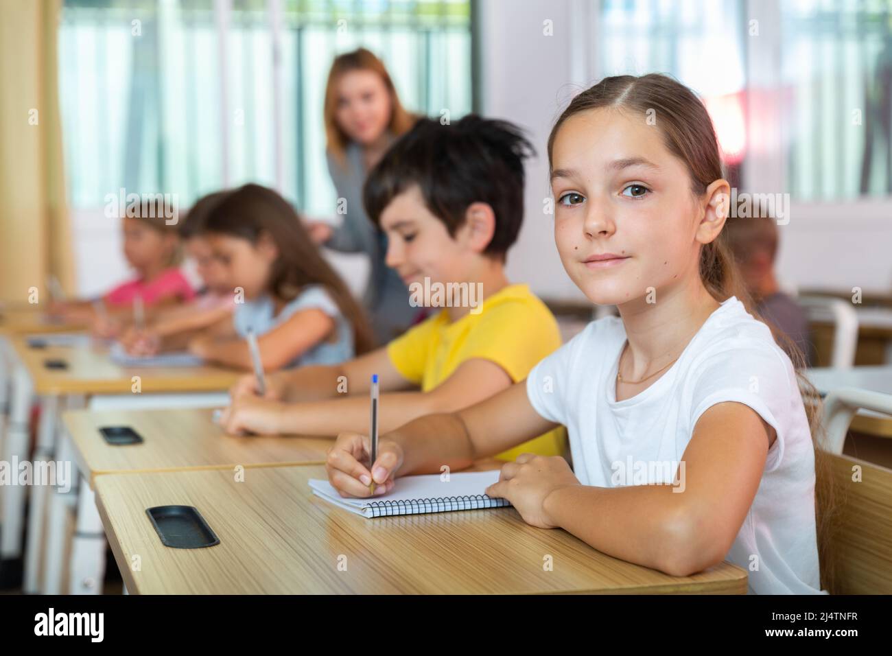 Smiling tween schoolgirl writing in workbook at lesson in class Stock ...