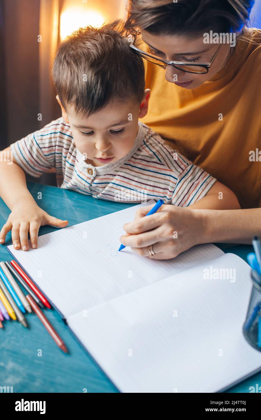 Caucasian little boy writing at home with his mother. Homework ...