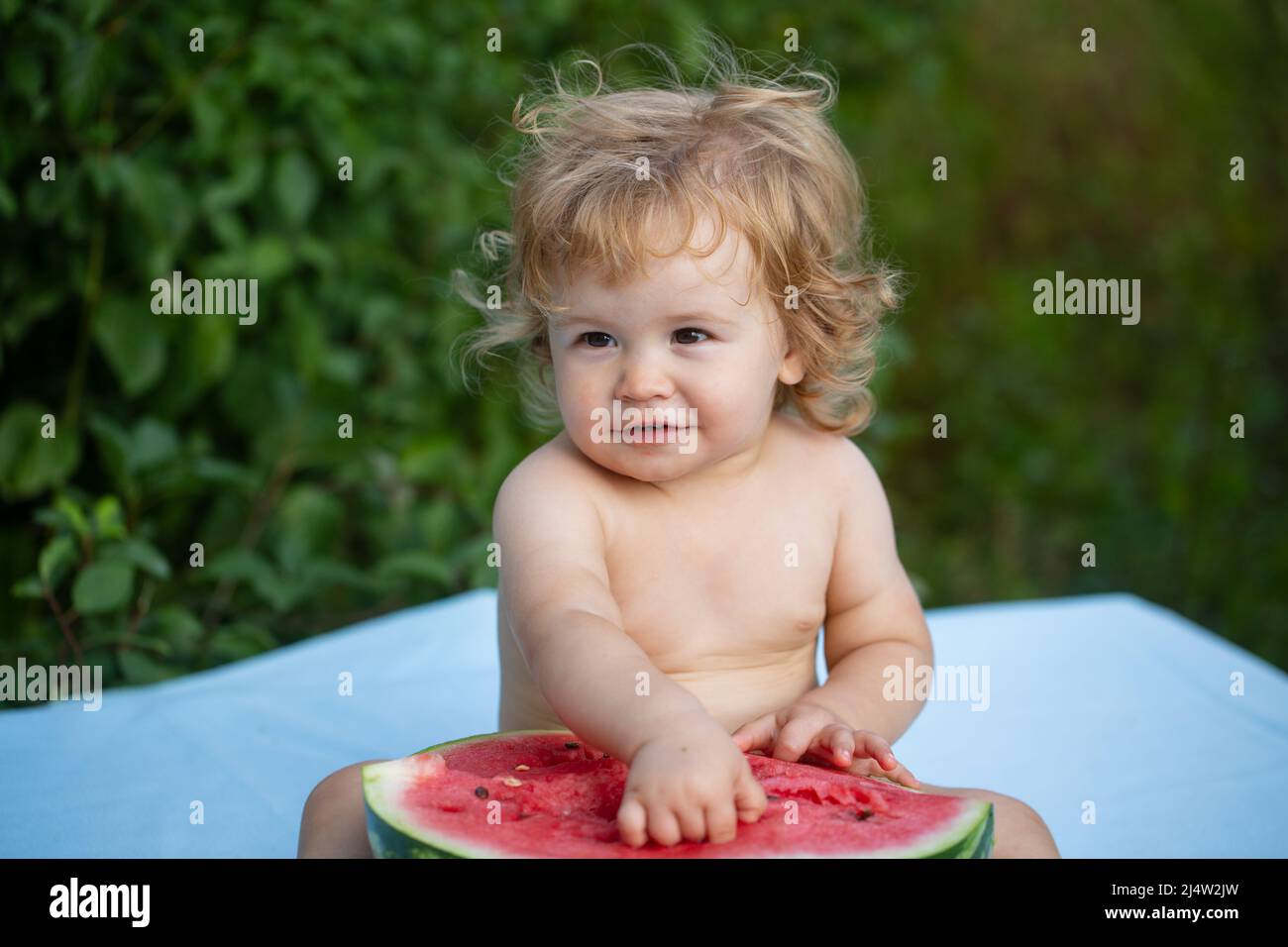 Little baby eating watermelon red in the garden sitting on the grass ...