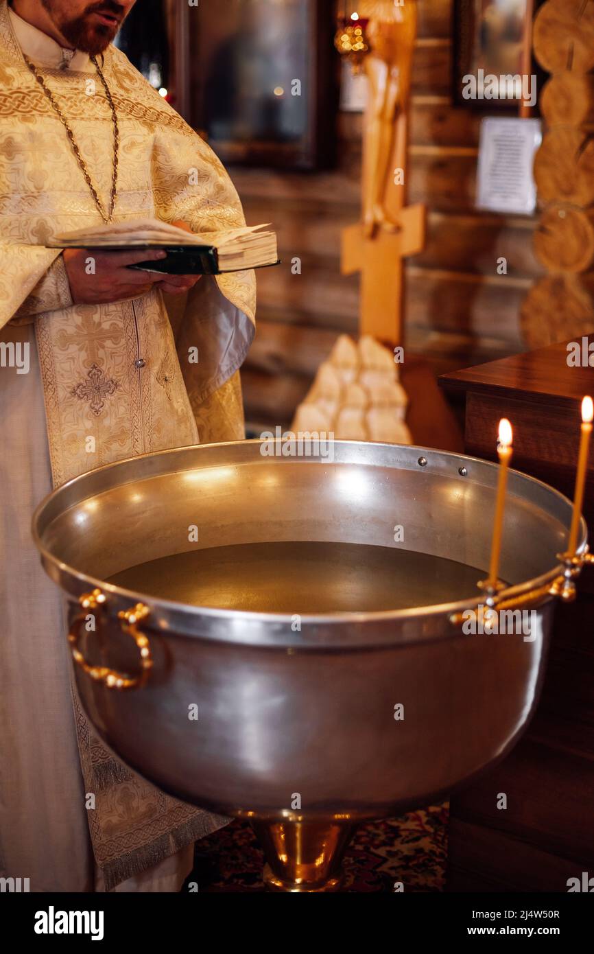 Unrecognizable bearded priest standing at font decorated with candles ...