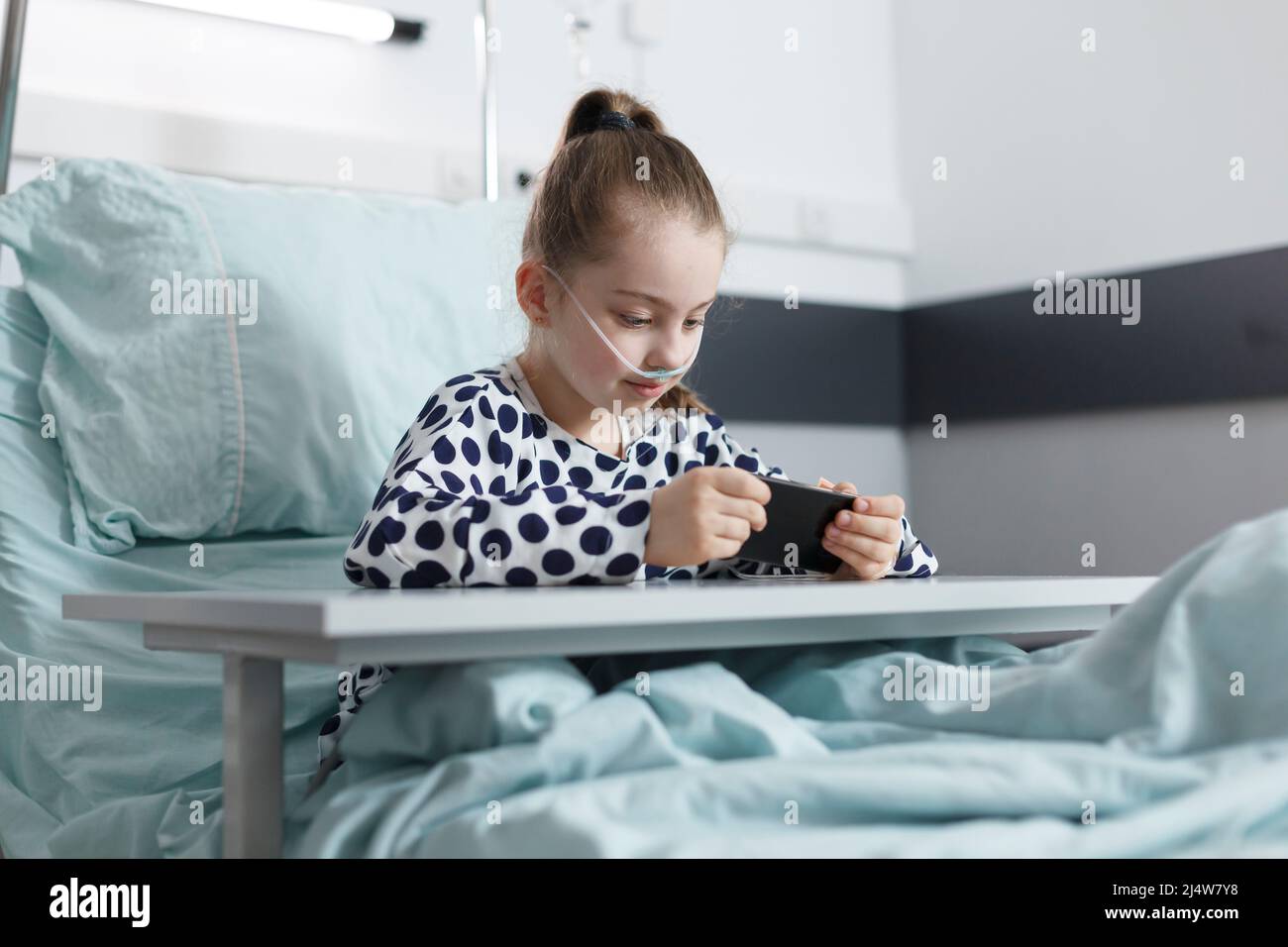 Cute little girl playing games on smartphone while resting on bed in ...