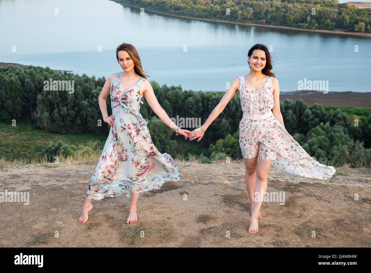 Pretty barefoot women in dresses pose on hill against river Stock Photo ...