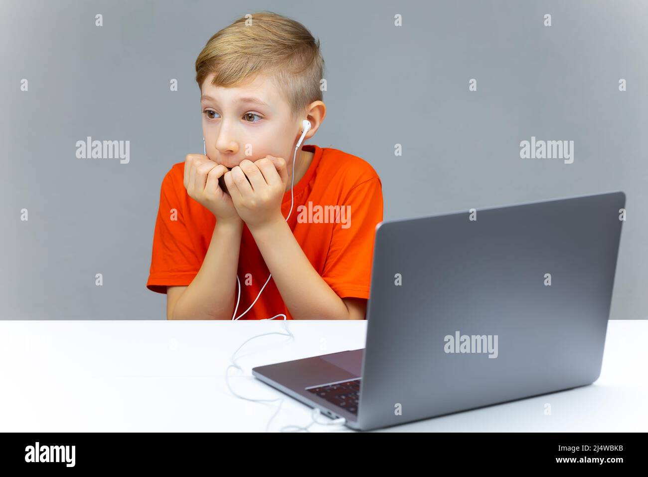 a boy sitting at a laptop biting his nails in surprise he is scared ...