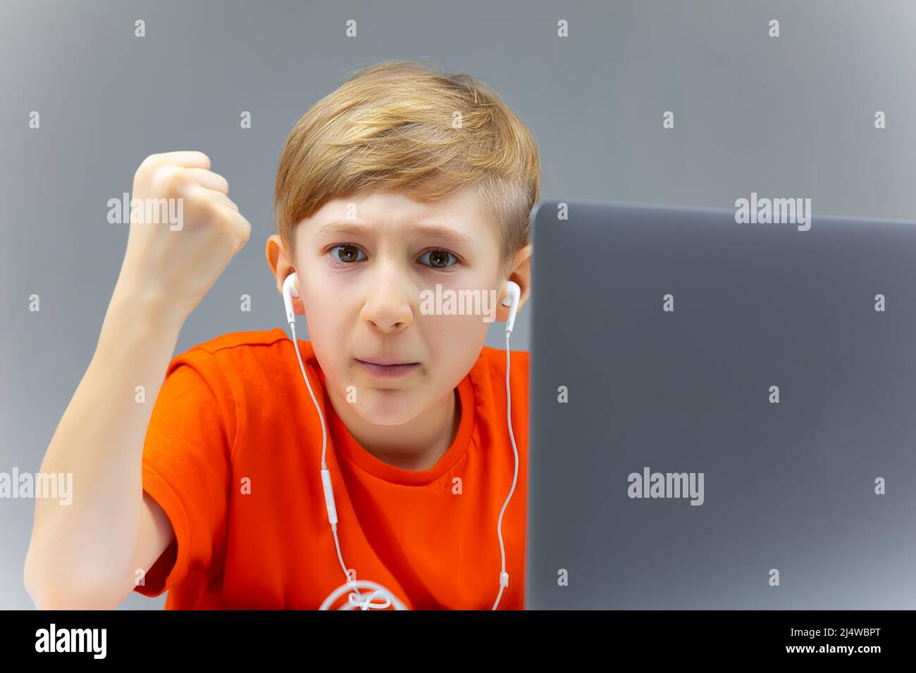 boy behind a laptop looks at the camera and shows his fist menacingly ...