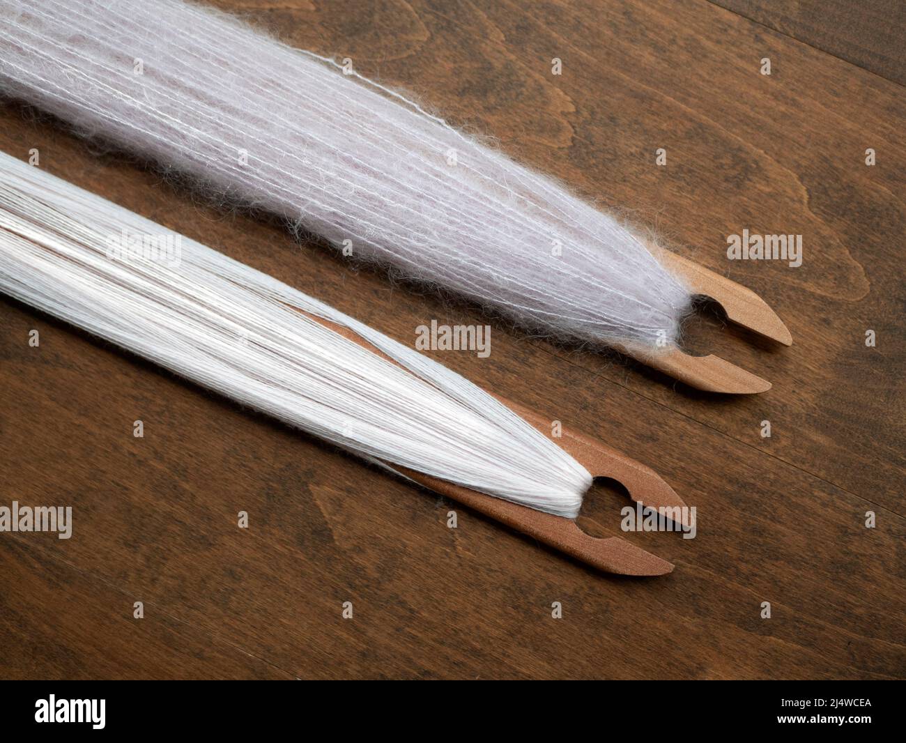 Weaving shuttles with light pink woolen and mohair threads on wooden ...
