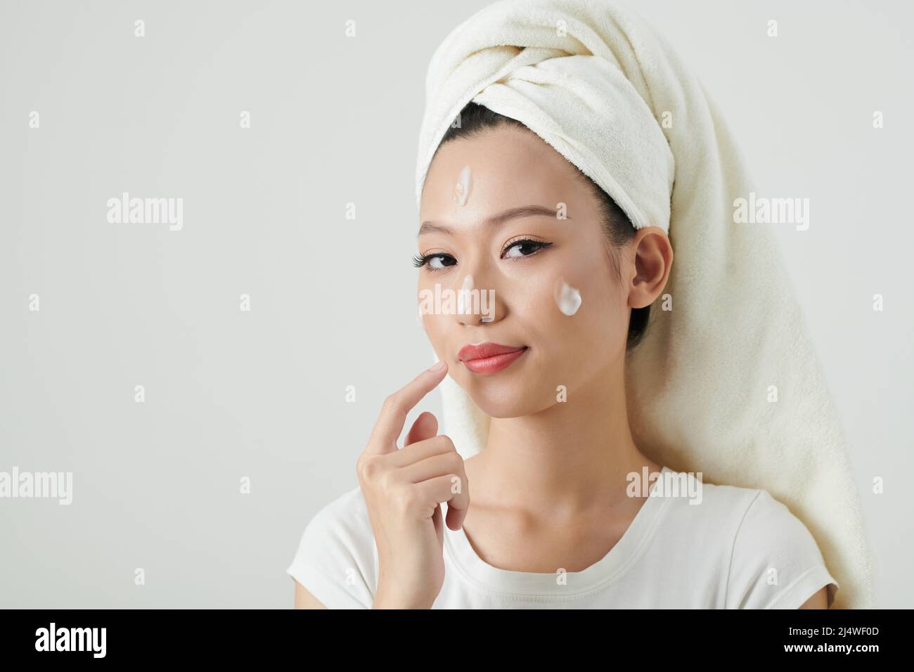 Positive young woman applying face cream to moisturize her skin after ...