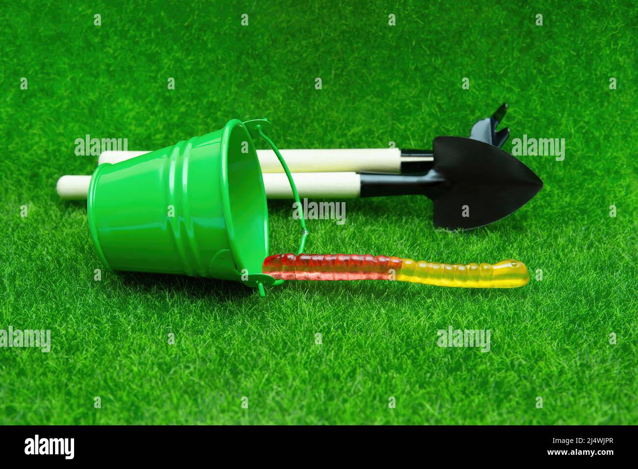 Miniature spade and rake with a small green bucket and a gummy worm on ...