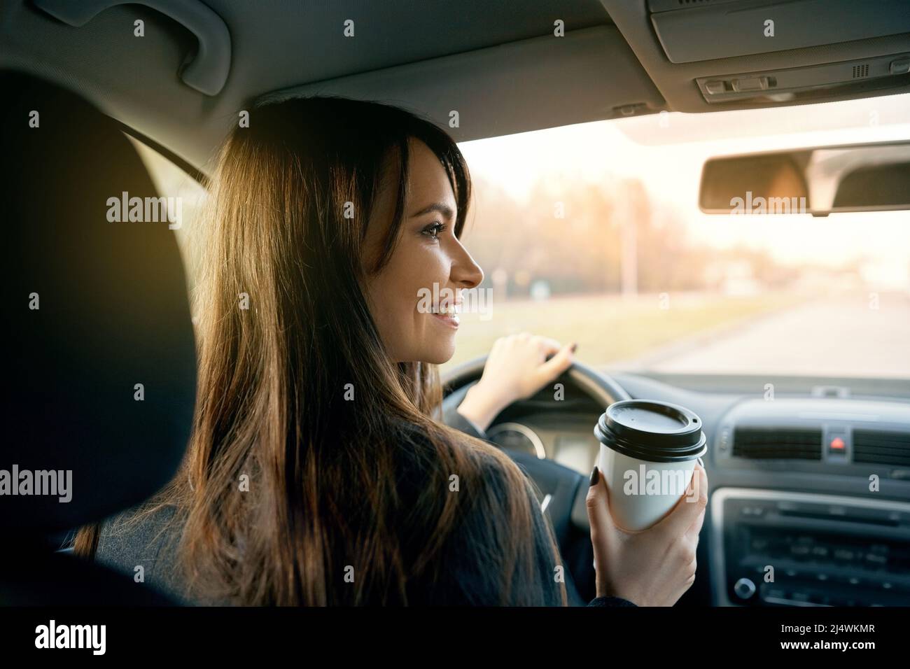 Beautiful woman holding steering wheel and coffee cup while driving a ...