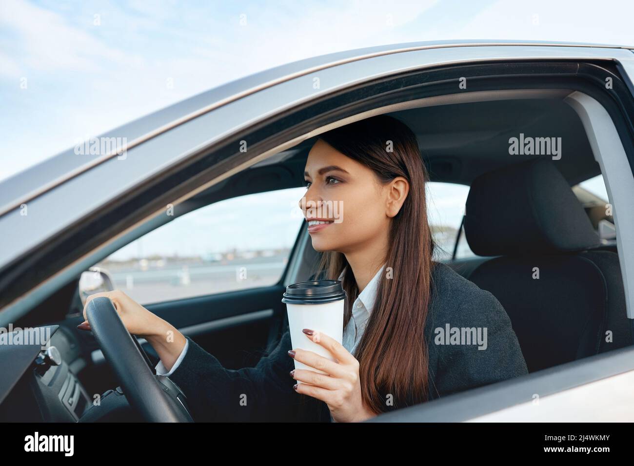 Happy young woman with coffee to go driving her car Stock Photo - Alamy