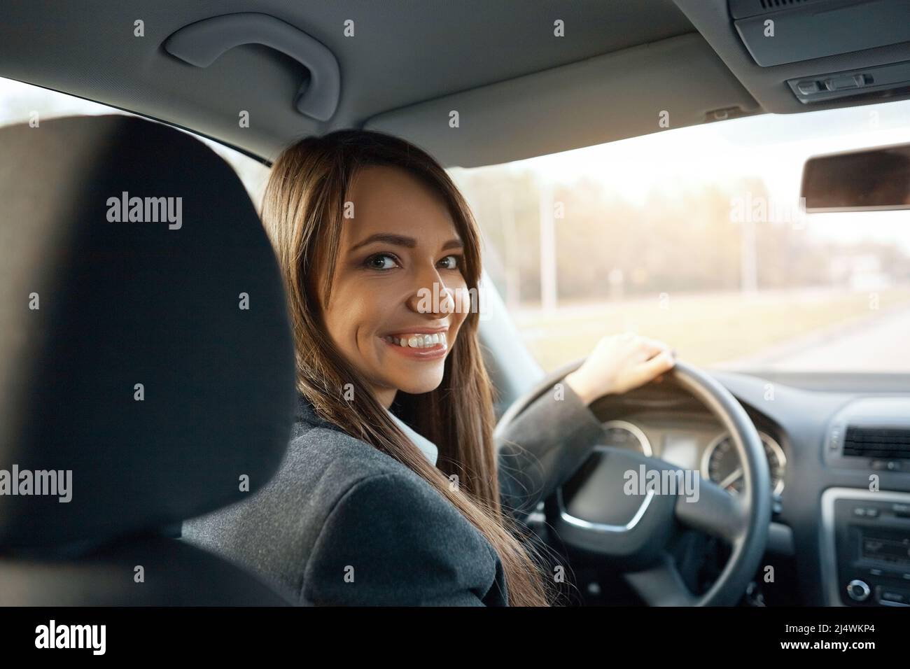 Driver turns to passenger seat and smiles at camera. Happy woman taxi ...