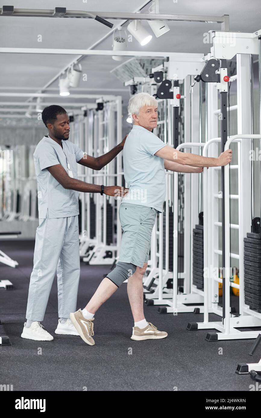 Full length portrait of senior man doing physiotherapy exercises in gym ...