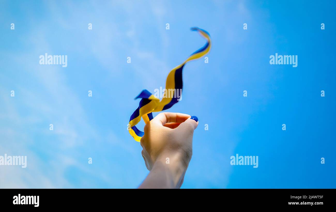 Hand holds blue yellow ribbon on sky background. Flag of Ukraine ...