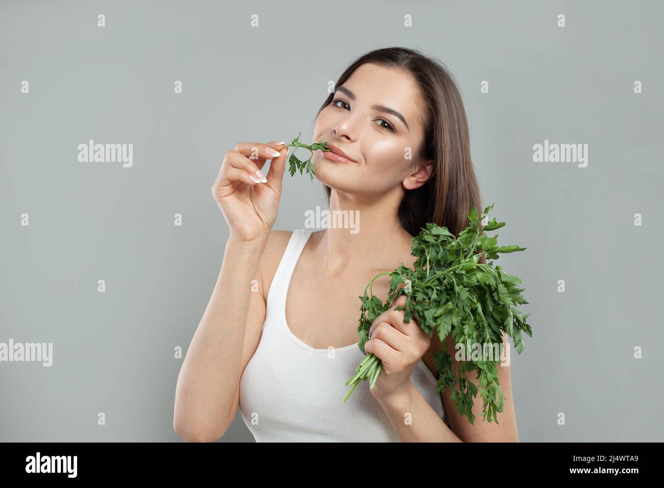 Attractive smiling woman eating salat parsley on white studio ...