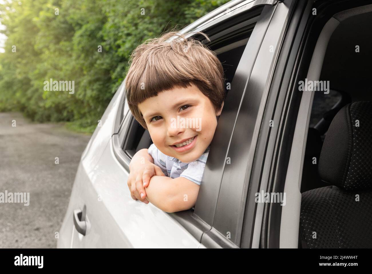Smiling little boy rides in car, looks out the open window, have fun ...