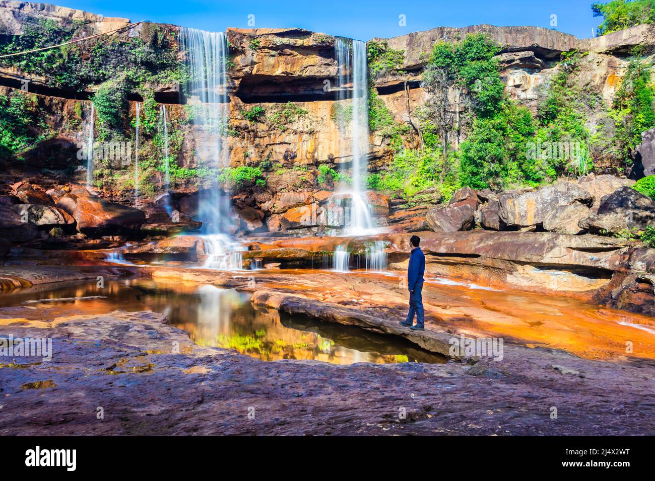 isolated young man watching waterfall falling from mountain top with ...