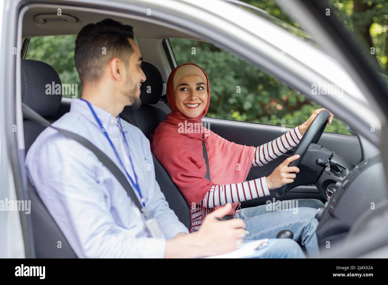 Smiling millennial middle eastern female in hijab at steering wheel ...