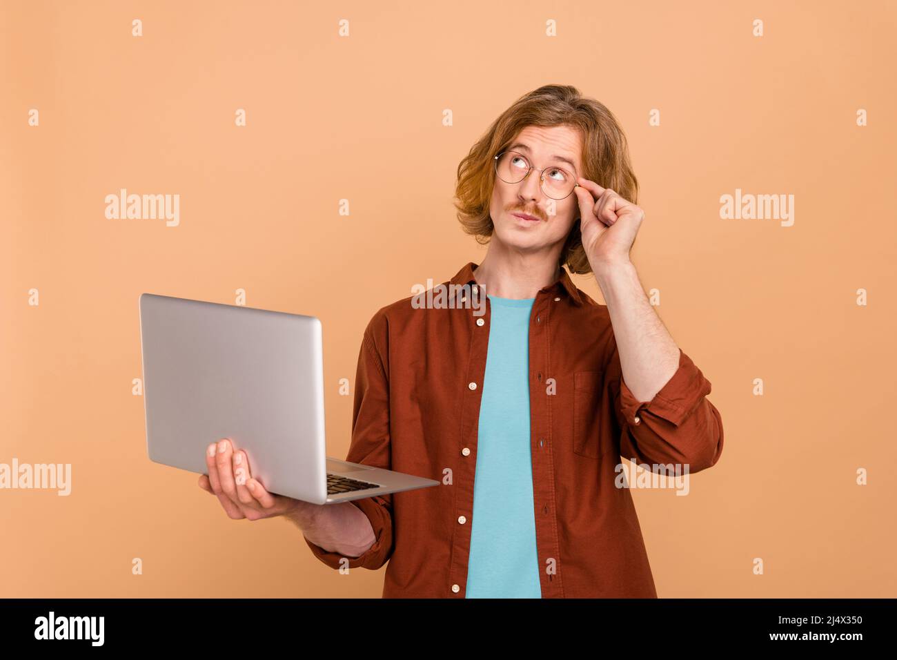Portrait of handsome minded trendy red-haired guy using laptop deciding ...