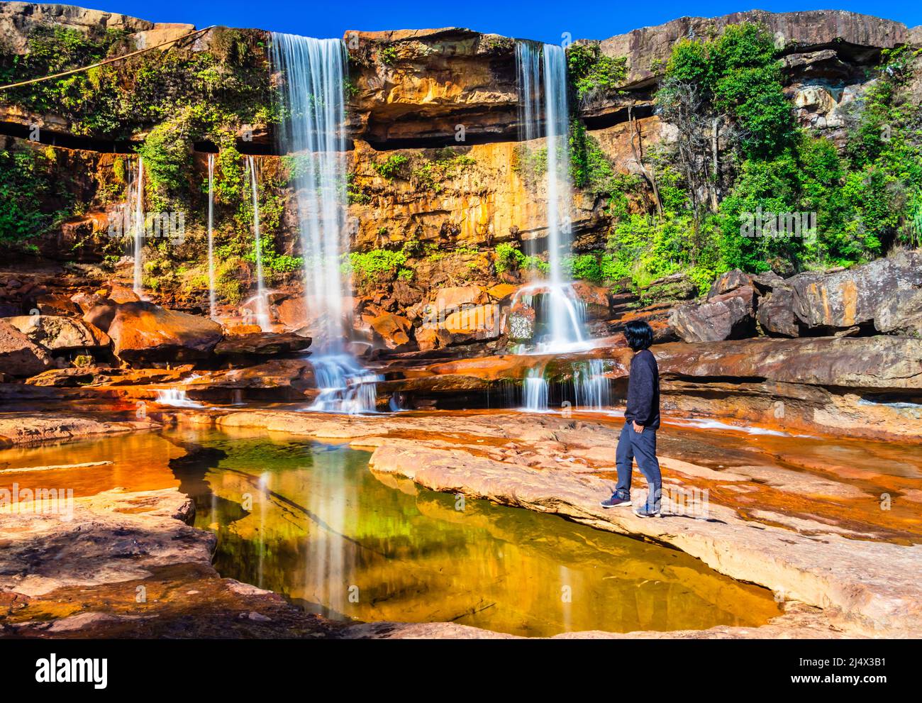 isolated young man watching waterfall falling from mountain top with ...