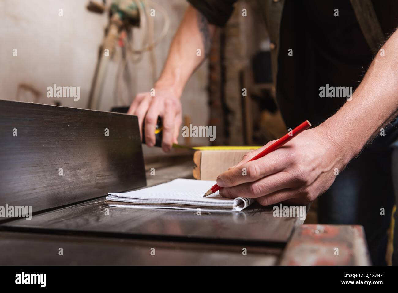 cropped view of carpenter writing in notebook while working in workshop ...