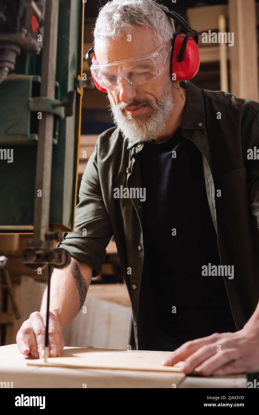bearded carpenter in goggles cutting timber with band saw Stock Photo ...