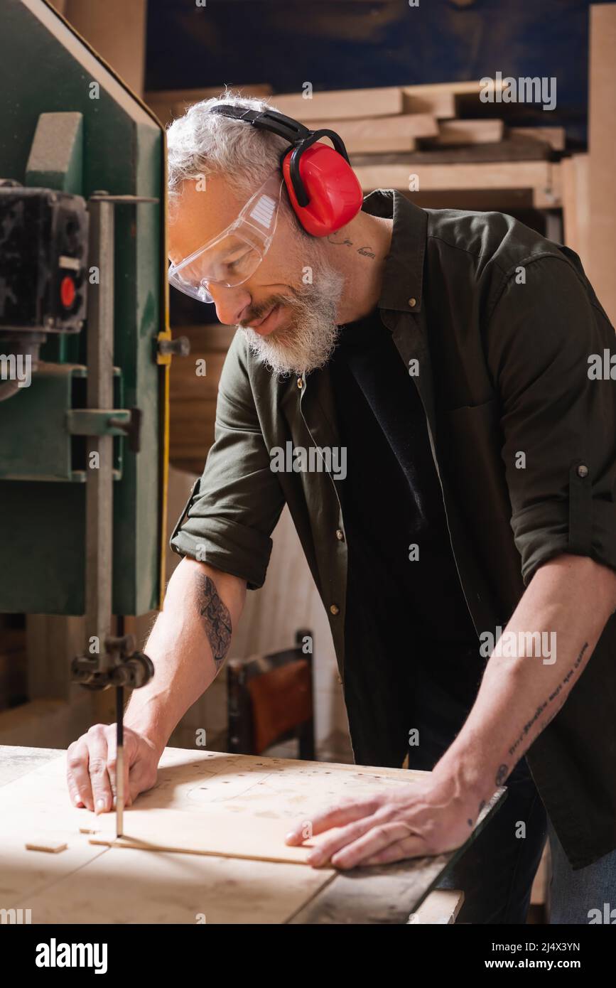 bearded carpenter in goggles cutting plywood with band saw Stock Photo ...