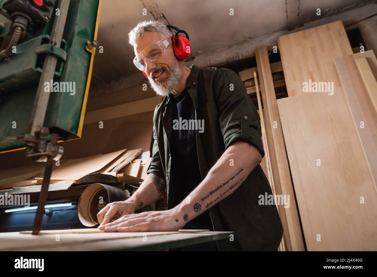 smiling carpenter cutting plywood on band saw in workshop Stock Photo ...