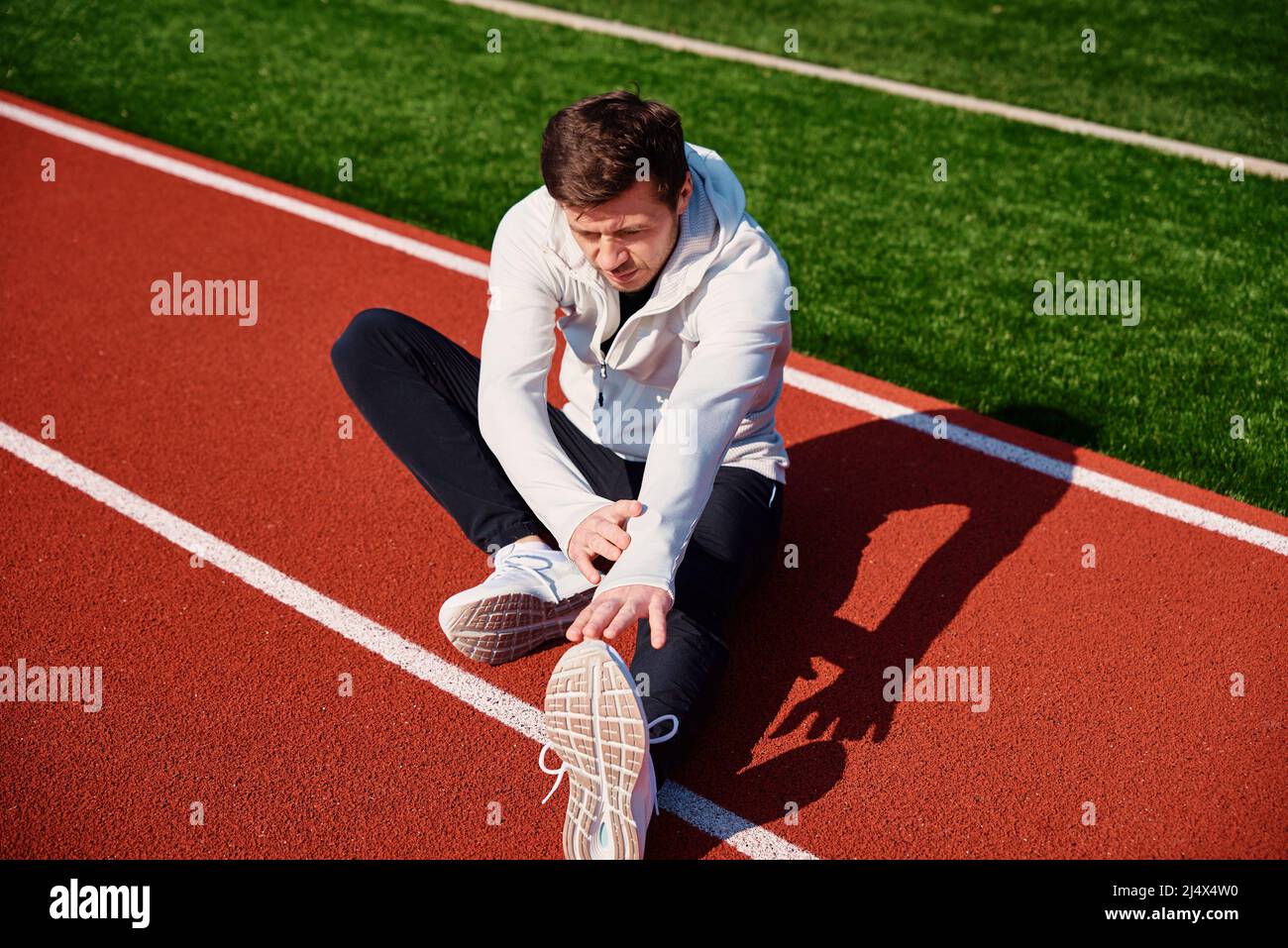 Man in sport clothers does a warm-up exercises at stadium track before ...