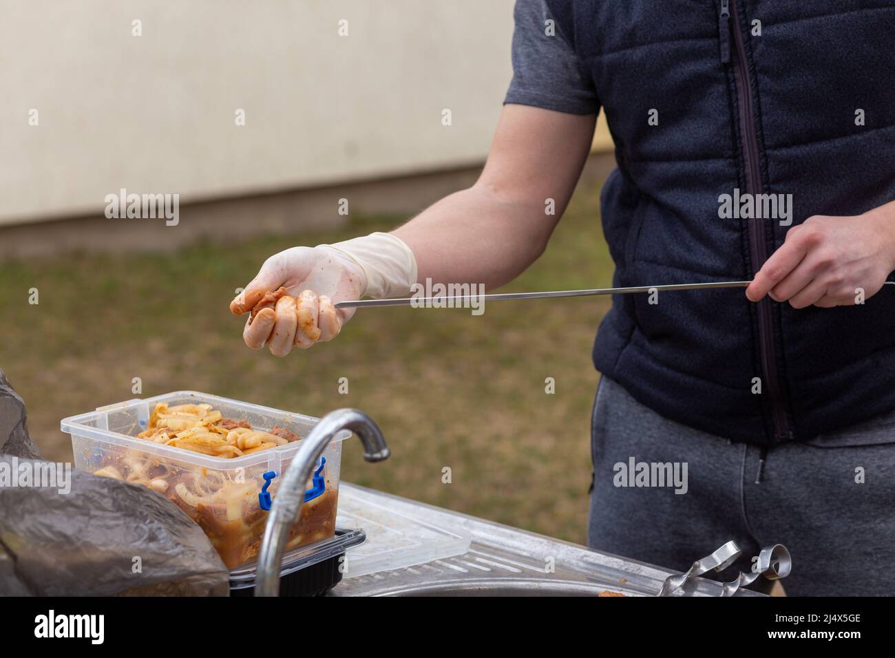 Male hands in white gloves stringing raw meat in marinade on skewers ...