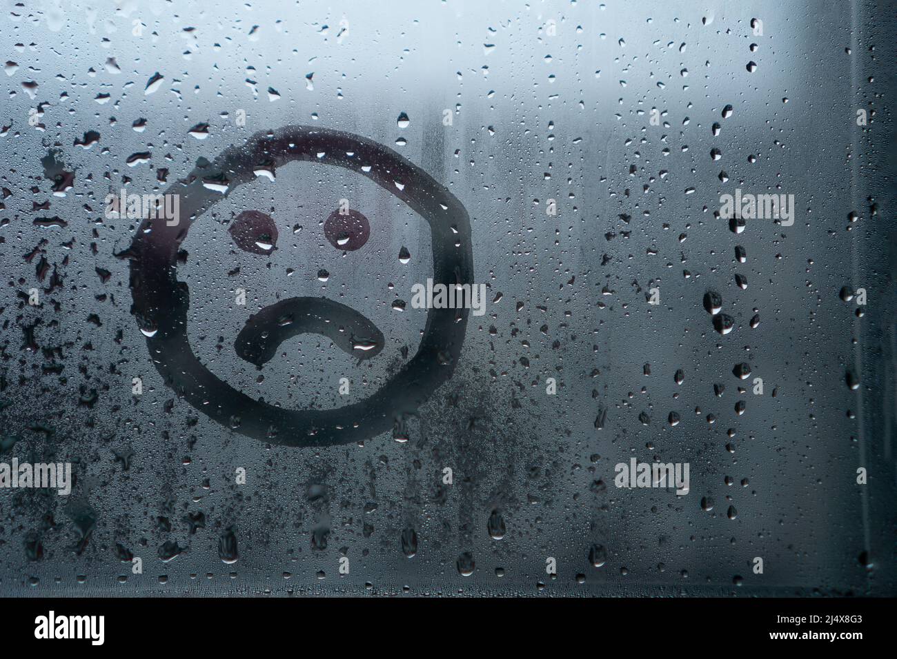 Sad smiley drawn by hand on wet fogged glass from the rain, copy the ...