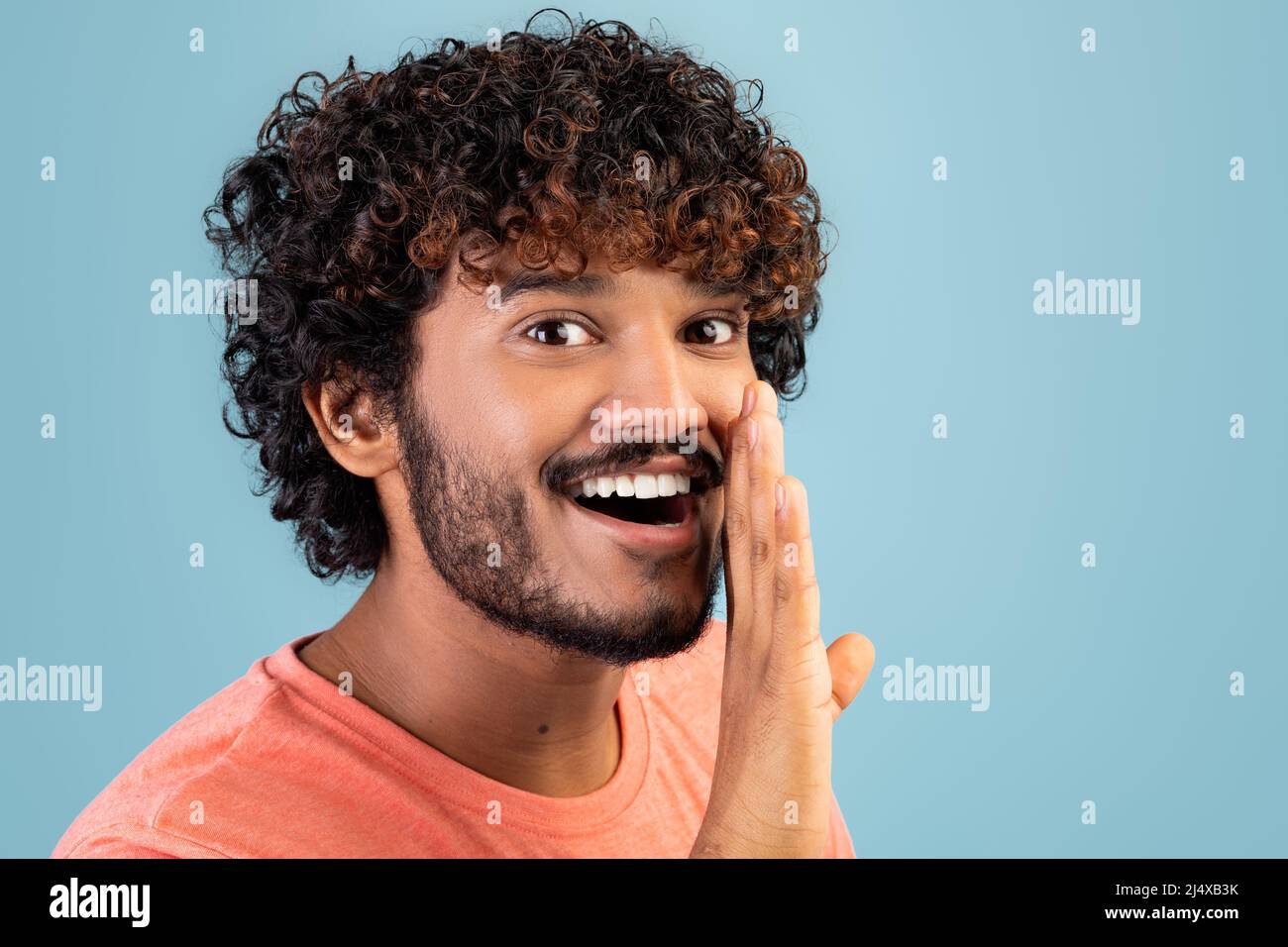 Positive eastern guy sharing secret on blue, copy space Stock Photo - Alamy