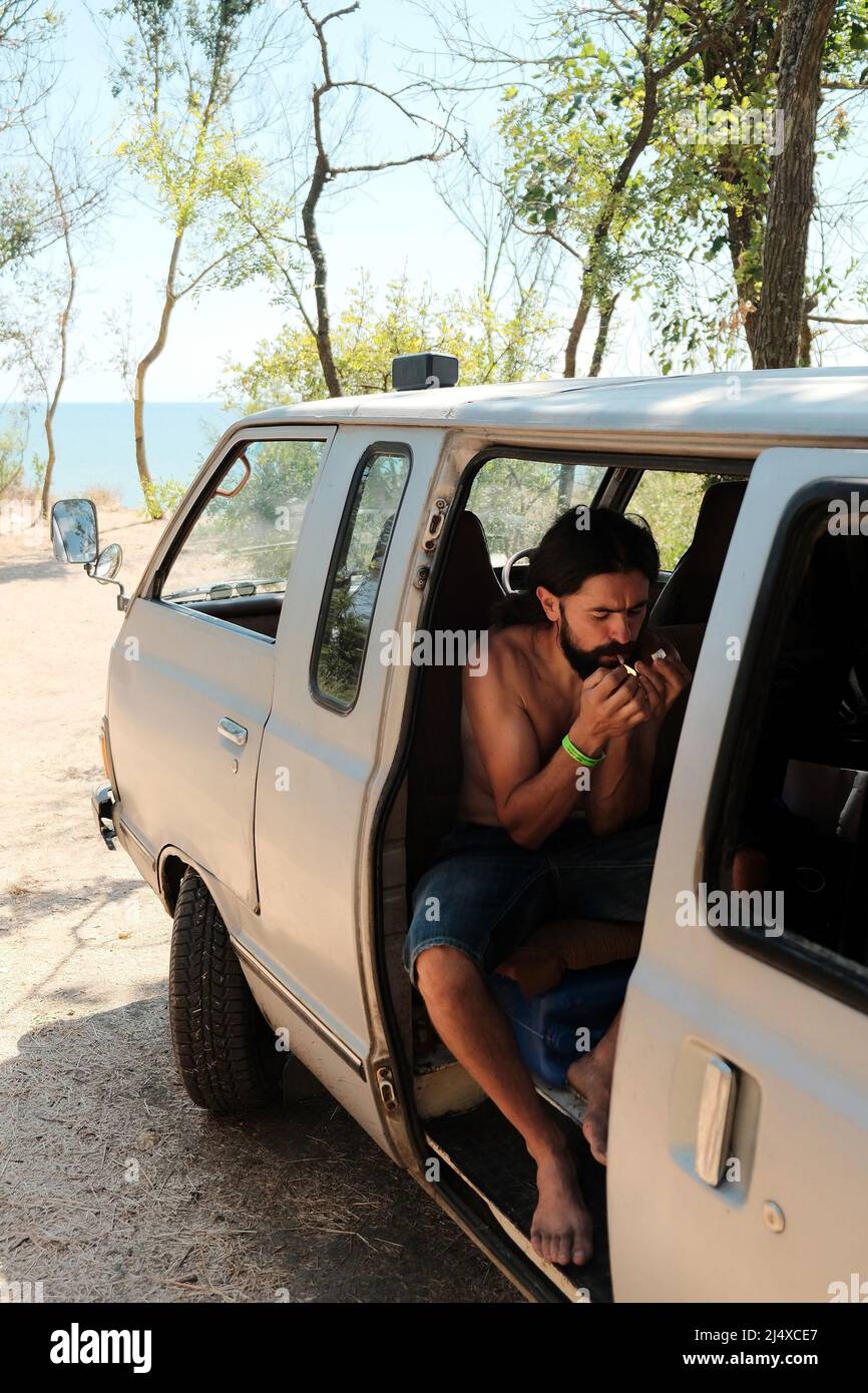Hippie man smoking cbd weed in a van at cannabis festival. Summer sea ...