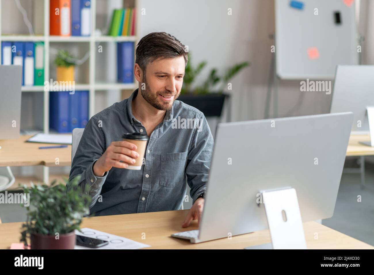 Happy mature businessman working on computer and drinking takeaway ...
