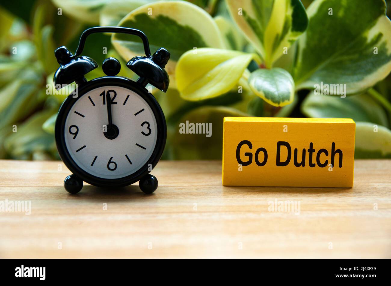 Alarm clock pointing at 12 o'clock with Go Dutch text on yellow wooden ...